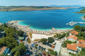 Vista aérea de uma área costeira com praia, marina e edifícios ao redor.