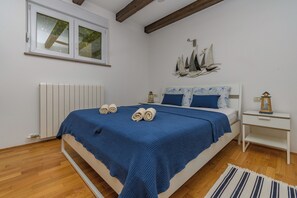 Quarto com cama, mesa de cabeceira, radiador, janela e um enfeite na parede.