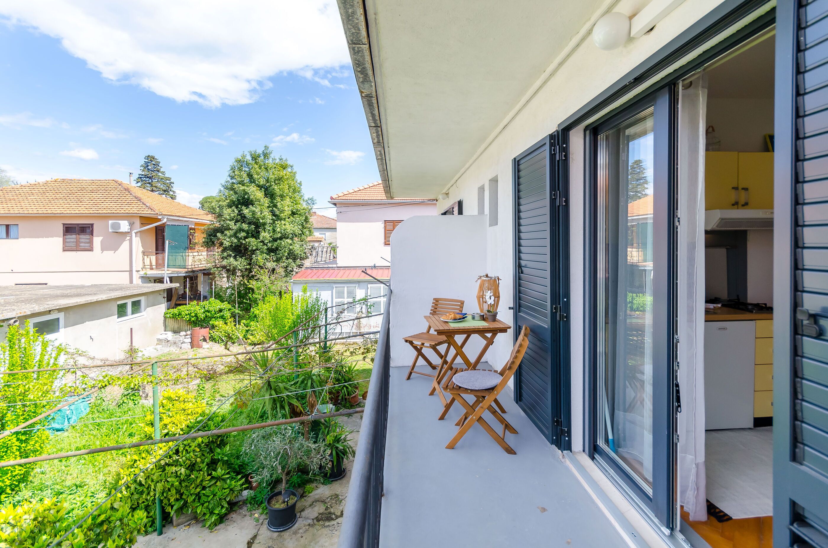 Varanda com mesa e cadeiras, porta de correr de vidro e vista para casas vizinhas.