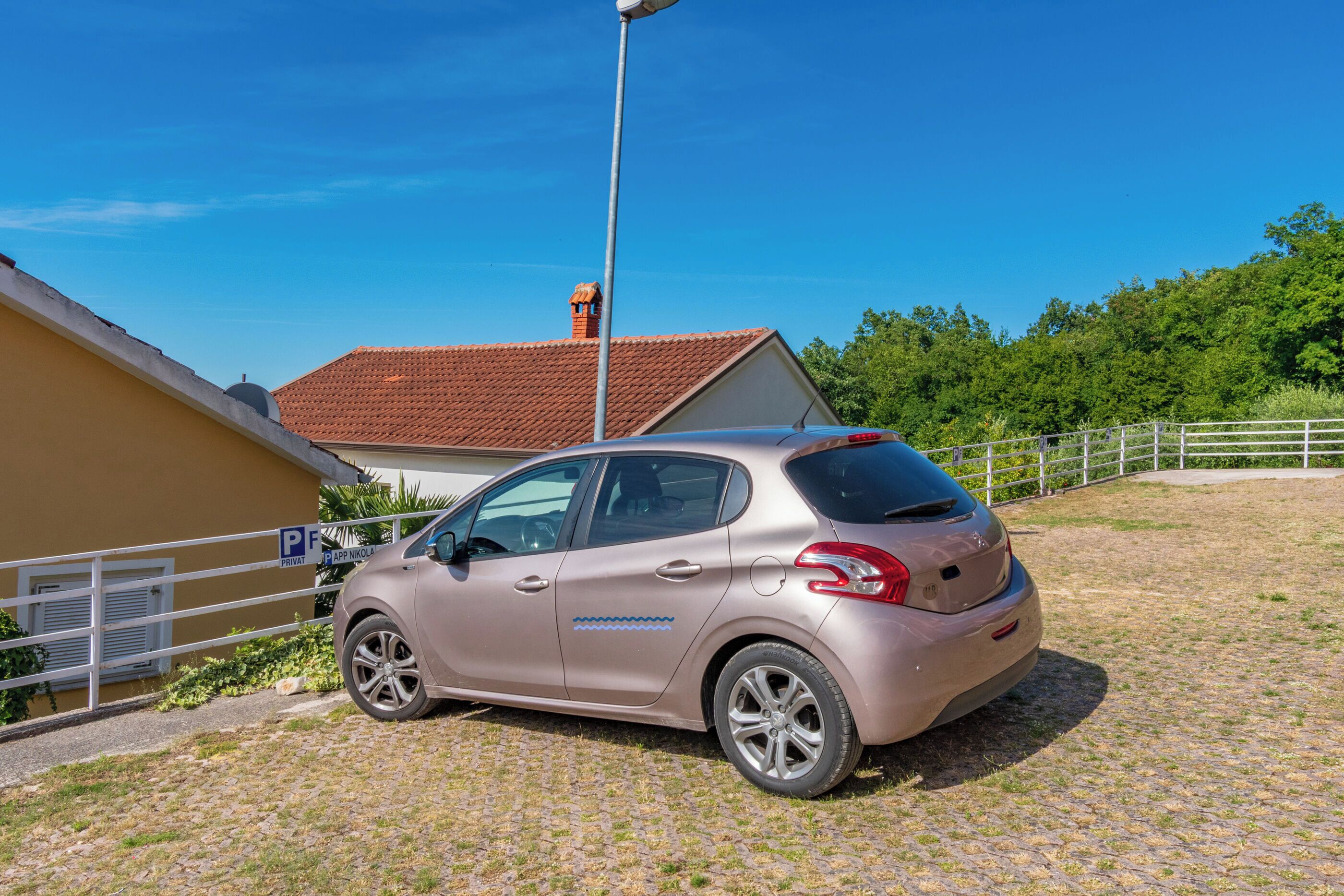 Um carro tipo hatchback bege estacionado em um caminho de paralelepípedos.