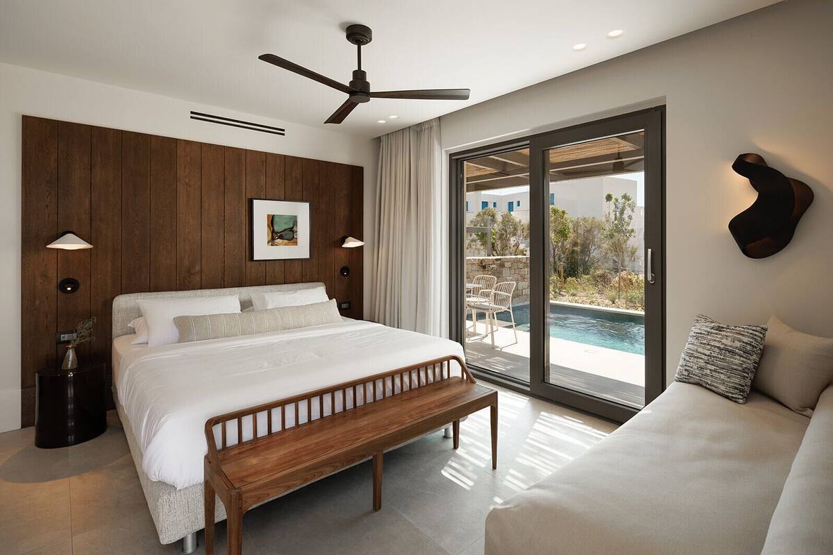 Quarto moderno com uma cama grande, um banco, um ventilador de teto e vista para uma piscina ao ar livre.