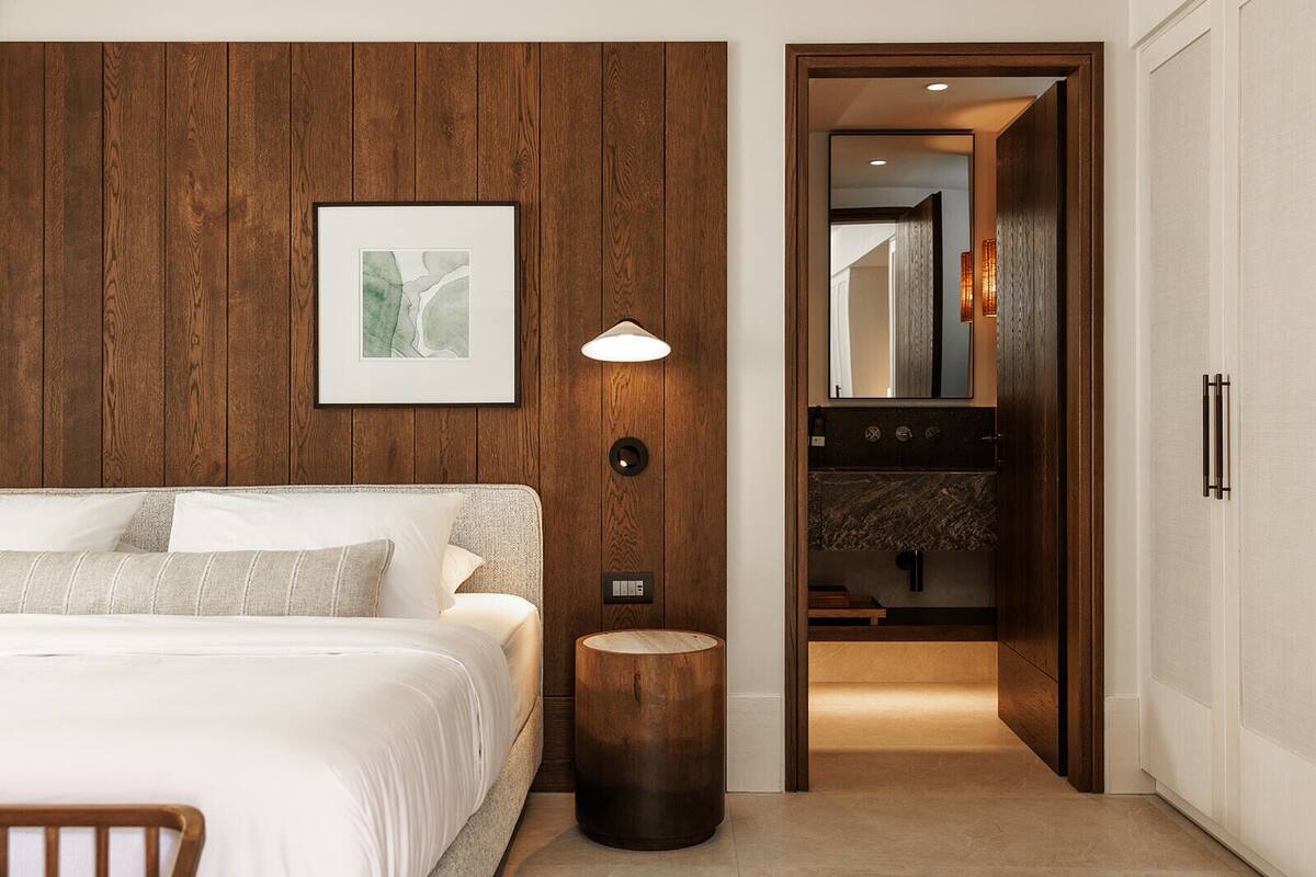Quarto com painel de parede de madeira, uma cama, abajur e um quadro emoldurado.