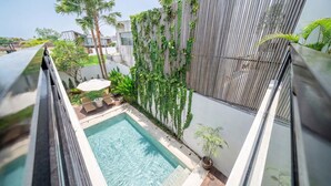 Piscina no terraço com vista para um edifício moderno, uma palmeira e um deque de madeira.