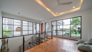 Um quarto espaçoso com grandes janelas, piso de madeira, escada com corrimão e ventilador de teto.