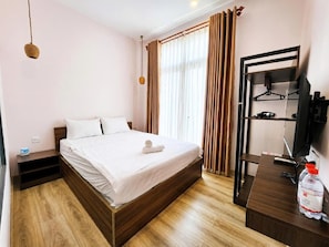 Quarto de hotel com cama de madeira, televisão de tela plana, escrivaninha com uma garrafa de água e espelho.