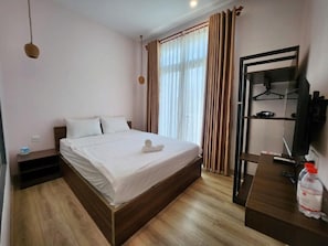 Quarto de hotel com cama de madeira, uma mesa com espelho, televisão e uma garrafa de água.