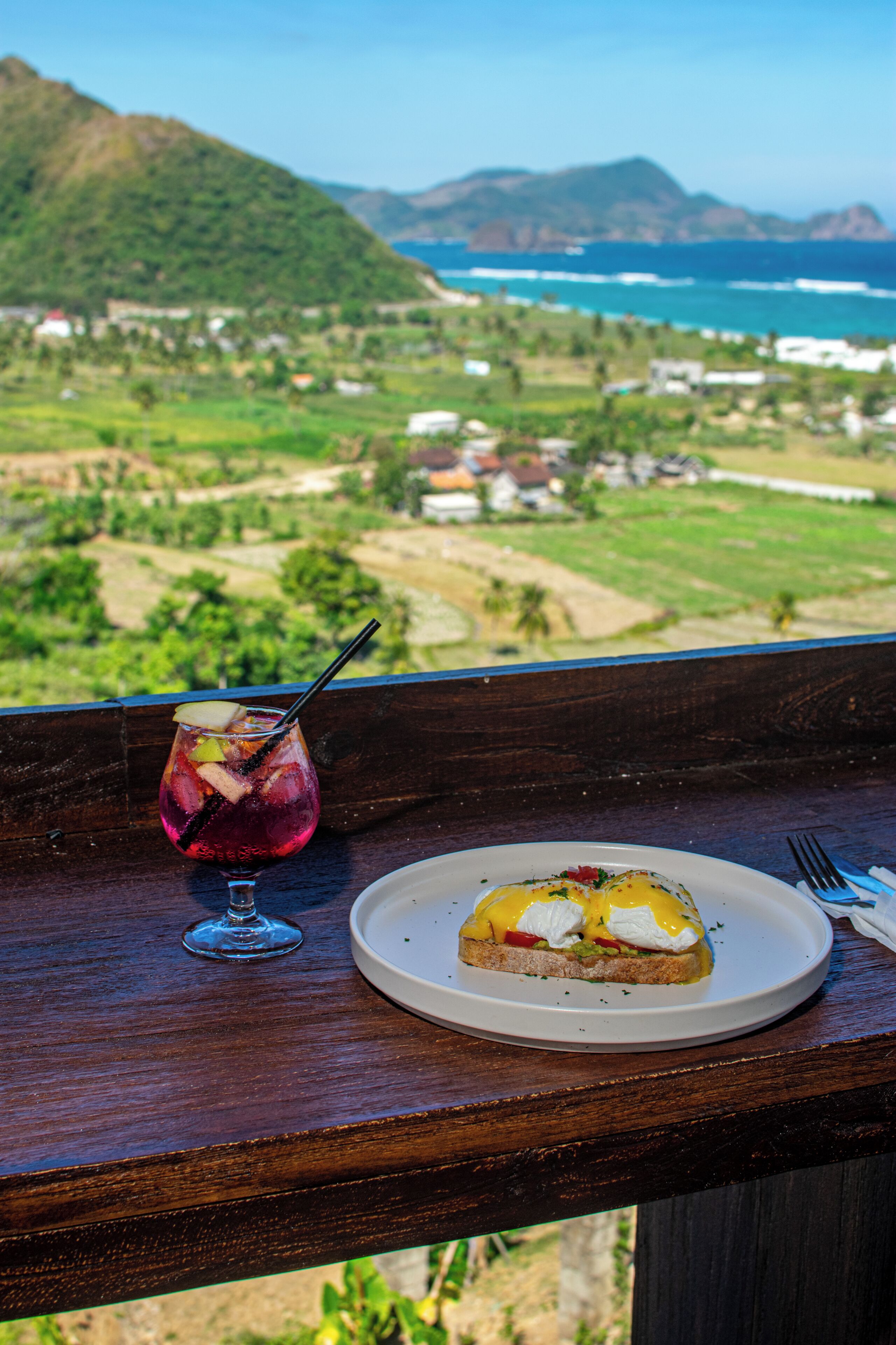 Uma mesa com um prato de comida e uma bebida, com vista para uma paisagem deslumbrante com montanhas e um corpo d'água.