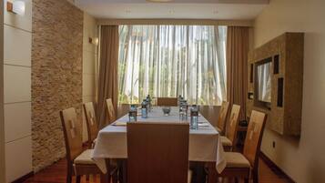Uma sala de conferências com uma mesa comprida, cadeiras, garrafas de água e uma janela grande com cortinas.