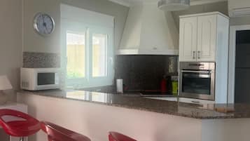 Cozinha equipada com micro-ondas, forno e relógio na parede. Três taboretes vermelhos.