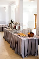 Disposição de buffet de café da manhã, com uma mesa comprida, dispensadores de bebidas e uma cesta de frutas.