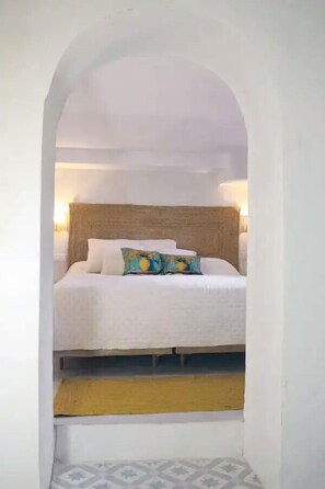 Cama com cabeceira de madeira, roupa de cama branca e almofada colorida.