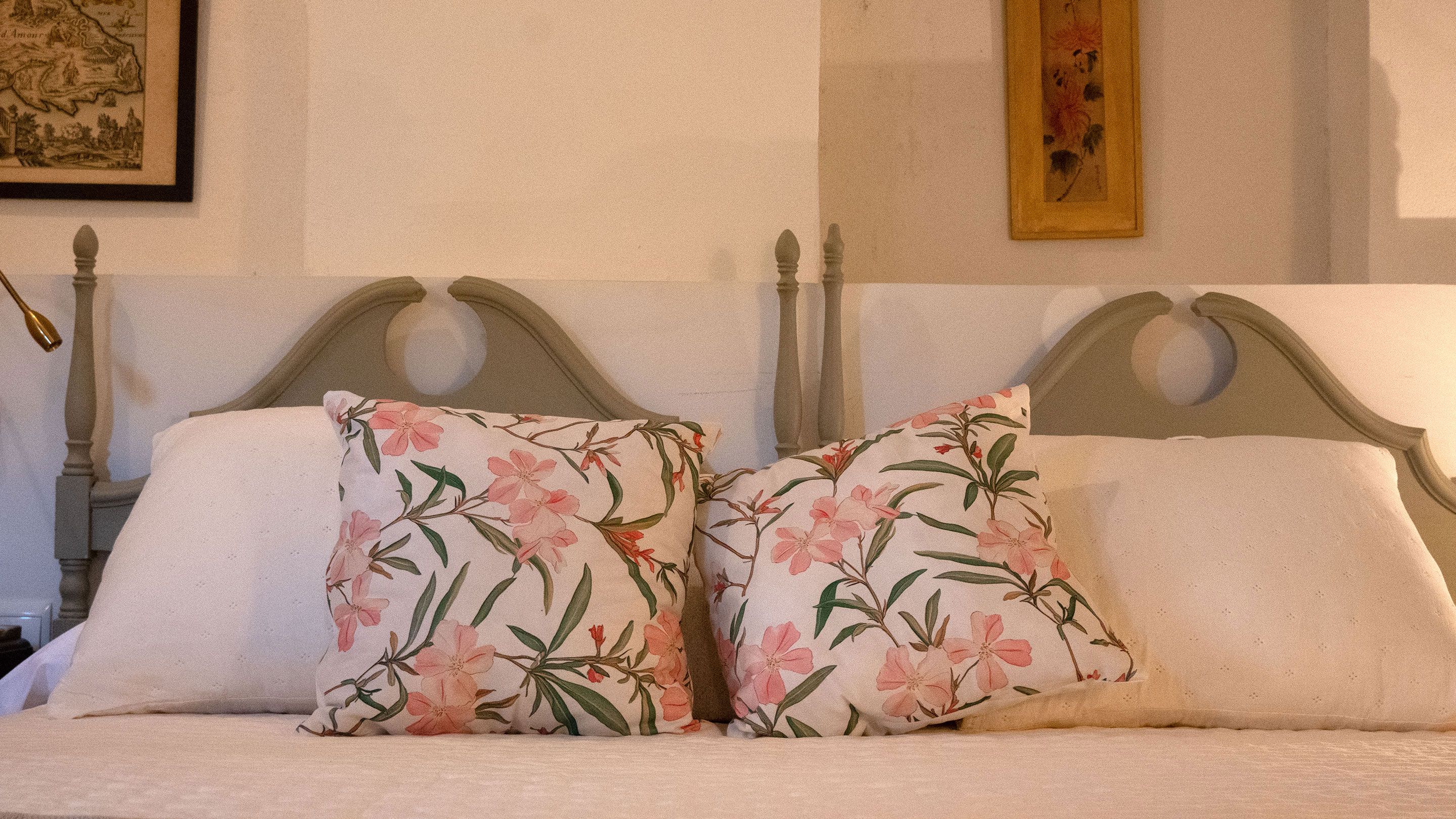 Uma cama com cabeceira, dois travesseiros estampados com flores e um quadro na parede.