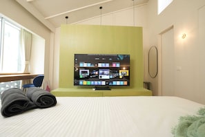 Quarto de hotel com cama, televisão montada numa parede verde e janela com cortinas.