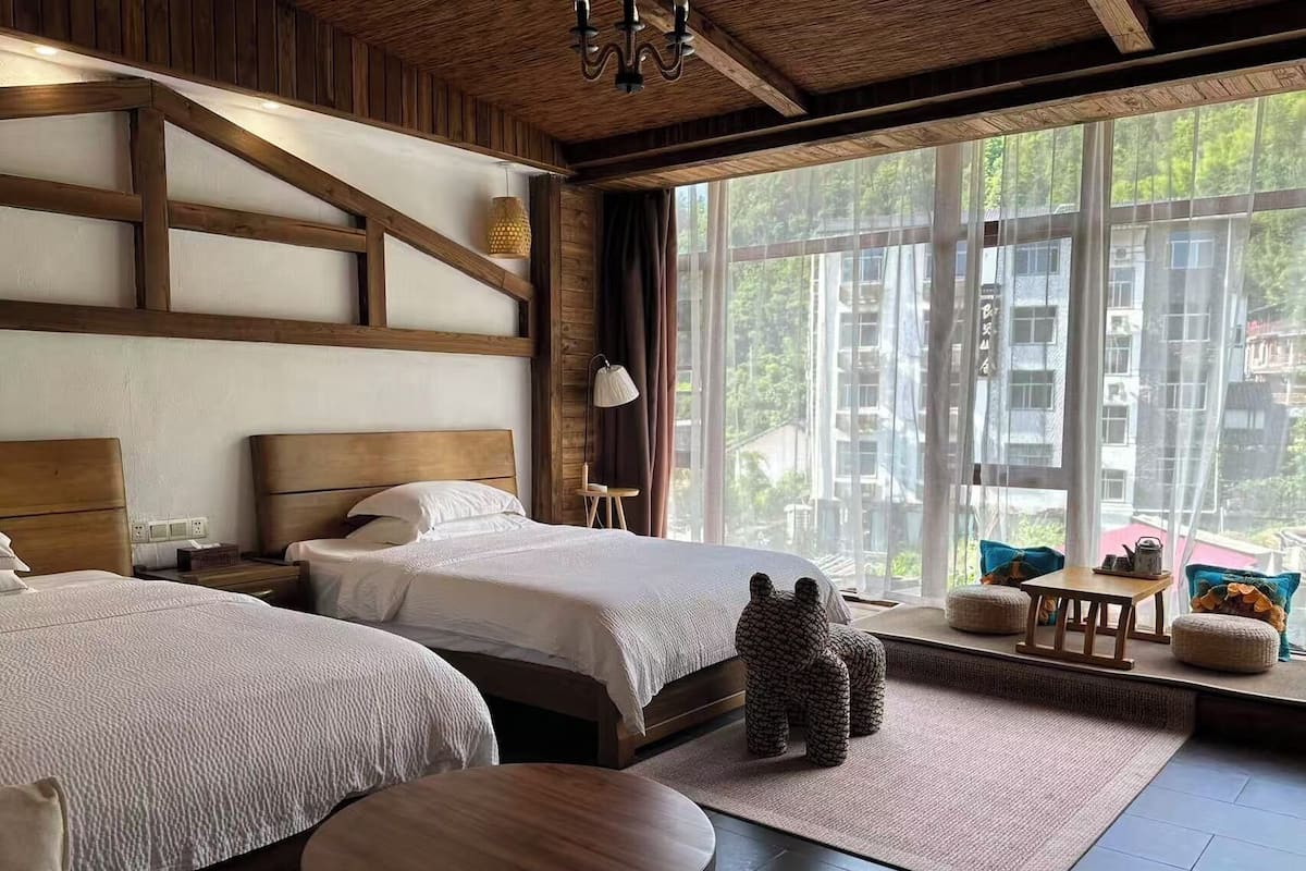 Quarto de hotel com duas camas, teto de madeira, uma janela ampla com vista e uma pequena mesa com abajur.