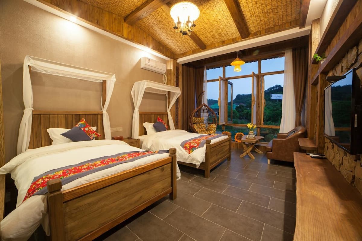 Quarto com duas camas de madeira, uma mesa pequena, um sofá e uma televisão.