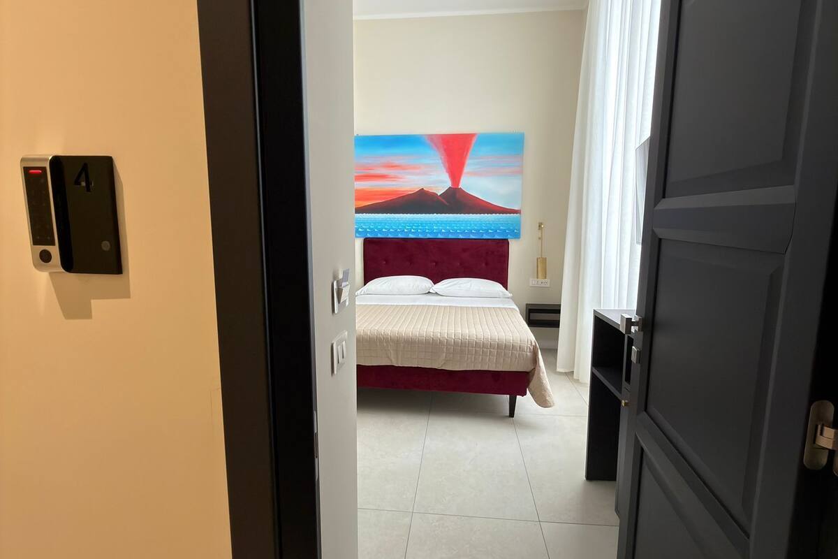 Quarto de hotel com cama, um quadro, uma porta e interruptor de luz.