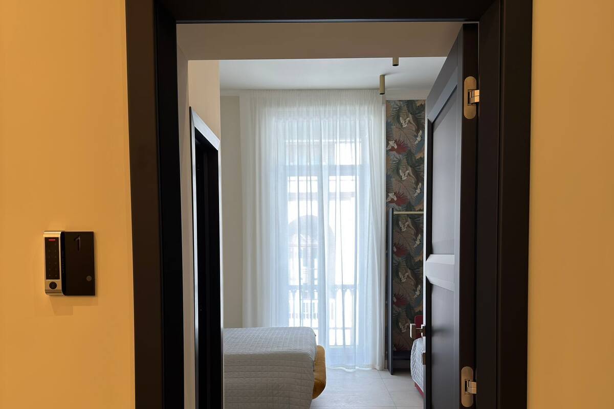 Corredor que leva a um quarto com cama, uma porta com puxador e um interruptor de luz na parede.