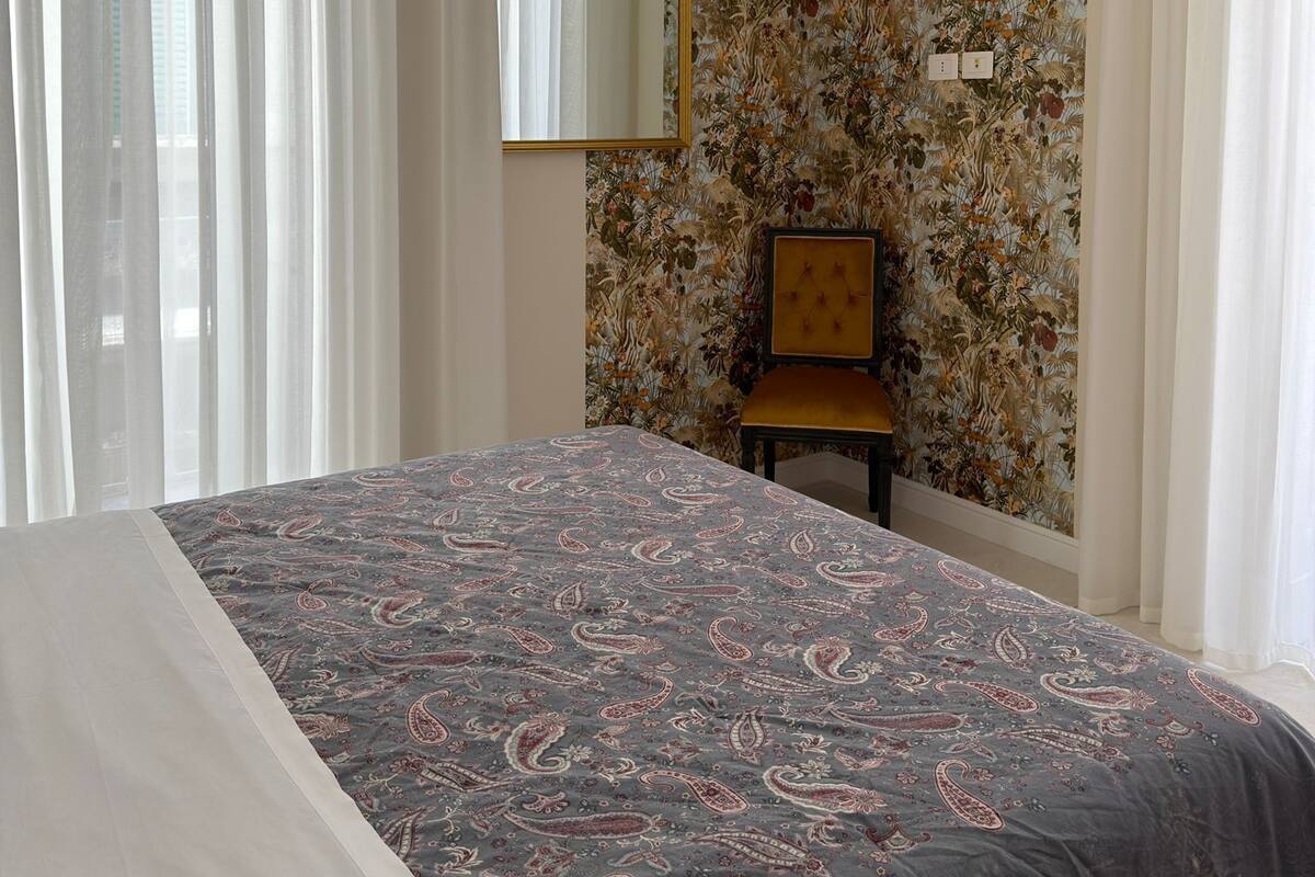 Quarto com cama, cadeira, espelho e papel de parede floral.