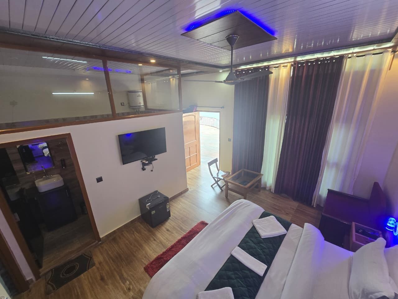 Quarto de hotel com cama, televisão, escrivaninha, cadeira e banheiro.