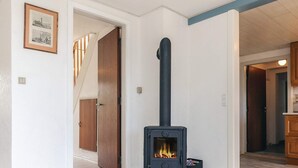 Um quarto com uma lareira a lenha preta, um quadro na parede e uma porta de madeira que dá para outro cômodo.