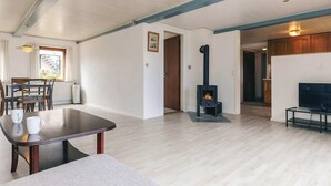 Uma sala de estar ampla com lareira, uma área de jantar com mesa e cadeiras, e uma televisão sobre um móvel.