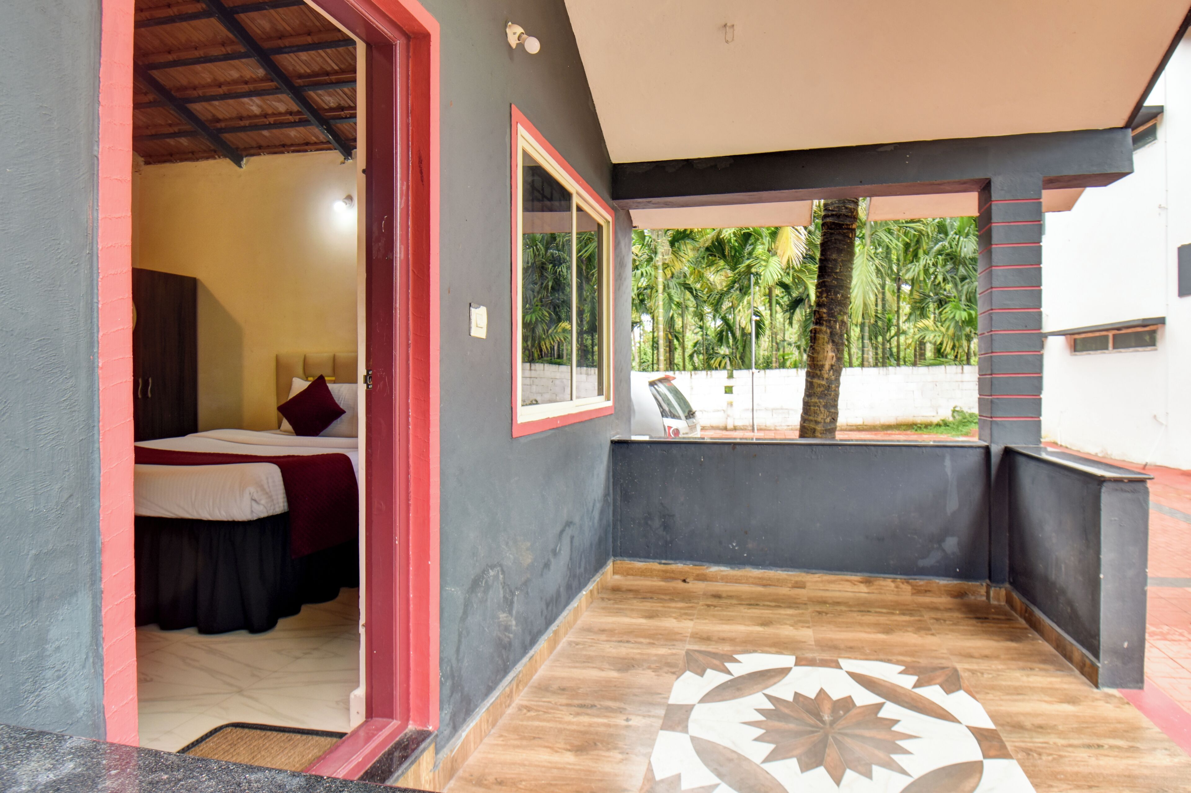 Quarto com cama, uma mesinha e vista para palmeiras pela janela.