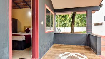 Quarto com cama, uma mesinha e vista para palmeiras pela janela.