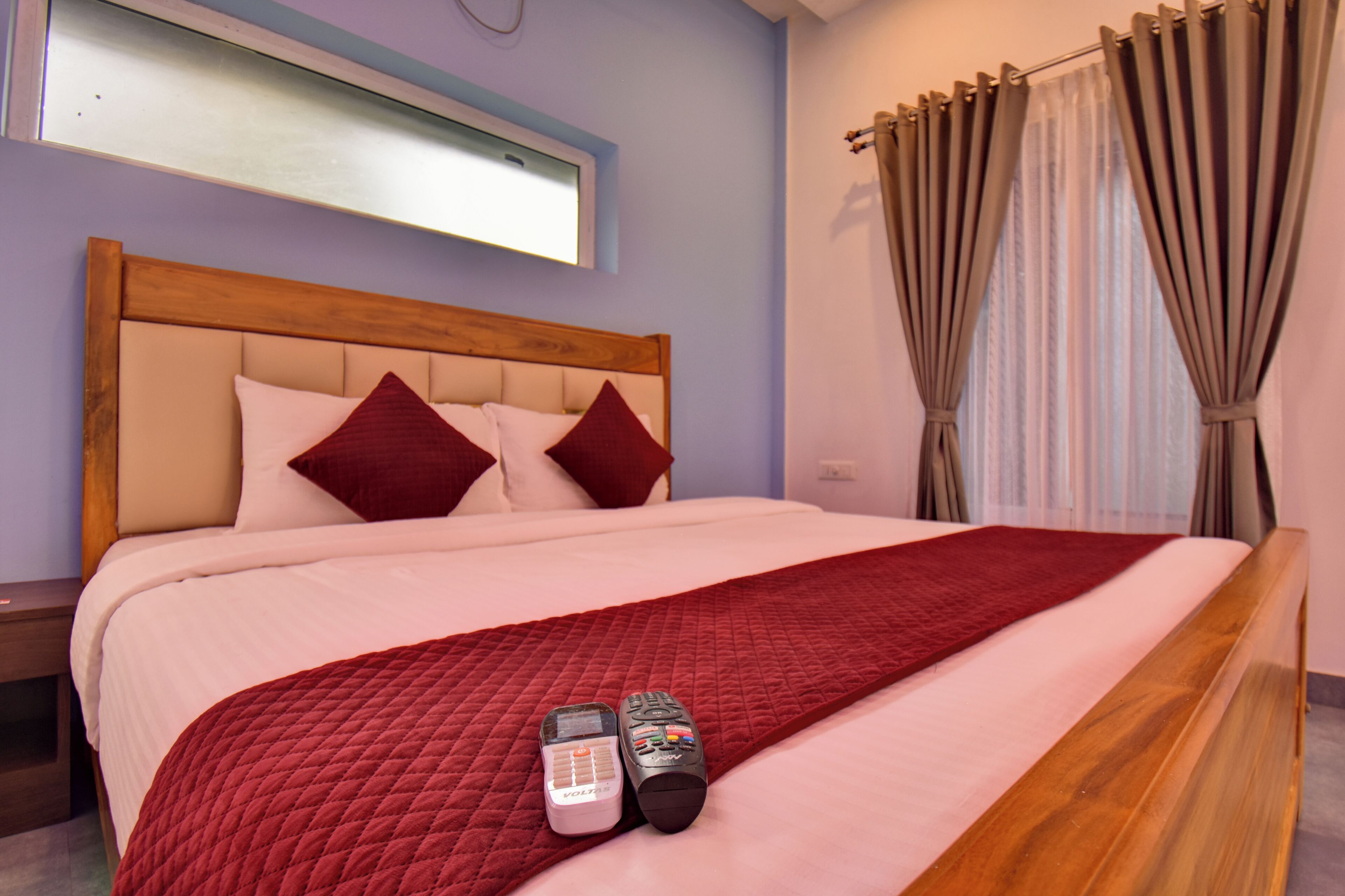 Quarto de hotel com cama, mesa de cabeceira, janela com persianas e cortina.