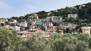 Zona residencial numa encosta, com vários edifícios altos, vegetação densa em primeiro plano e céu claro.