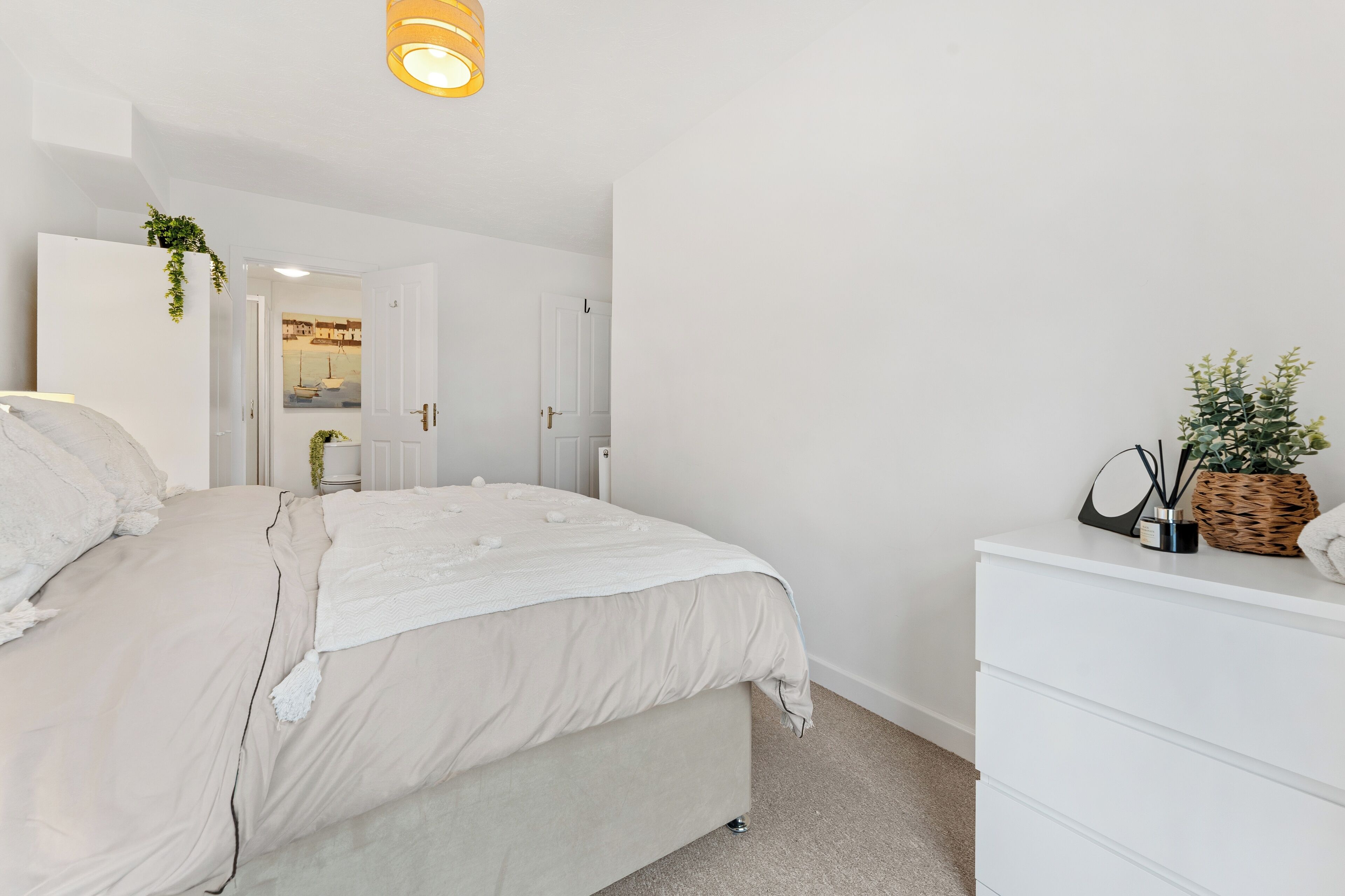 Quarto com cama, penteadeira e porta que dá para outro cômodo.