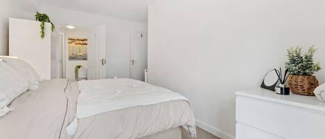 Quarto com cama, penteadeira e porta que dá para outro cômodo.