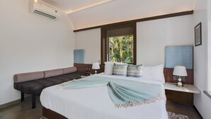 Quarto com cama, mesas de cabeceira, um banco e janela com vista para o verde.