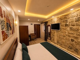 Quarto de hotel com cama, televisão, parede de pedra e um quadro na parede.