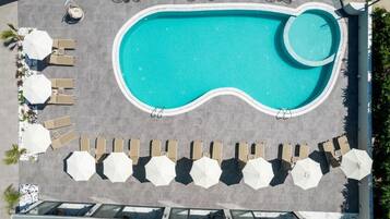 Vista aérea de uma piscina com formato peculiar, cercada por espreguiçadeiras e guarda-sóis.