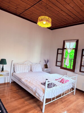 Um quarto com cama, mesas de cabeceira, abajur, janela com cortinas e teto de madeira.