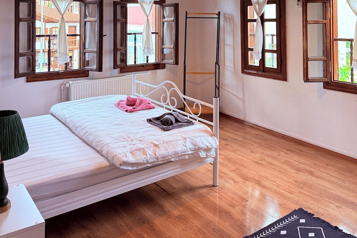 Quarto com cama, teto de madeira, janelas com cortinas e luminária pendente.