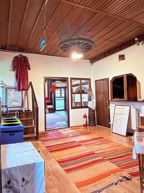Quarto de hotel com piso de madeira, tapete listrado e colorido, um extintor de incêndio e uma placa com texto.