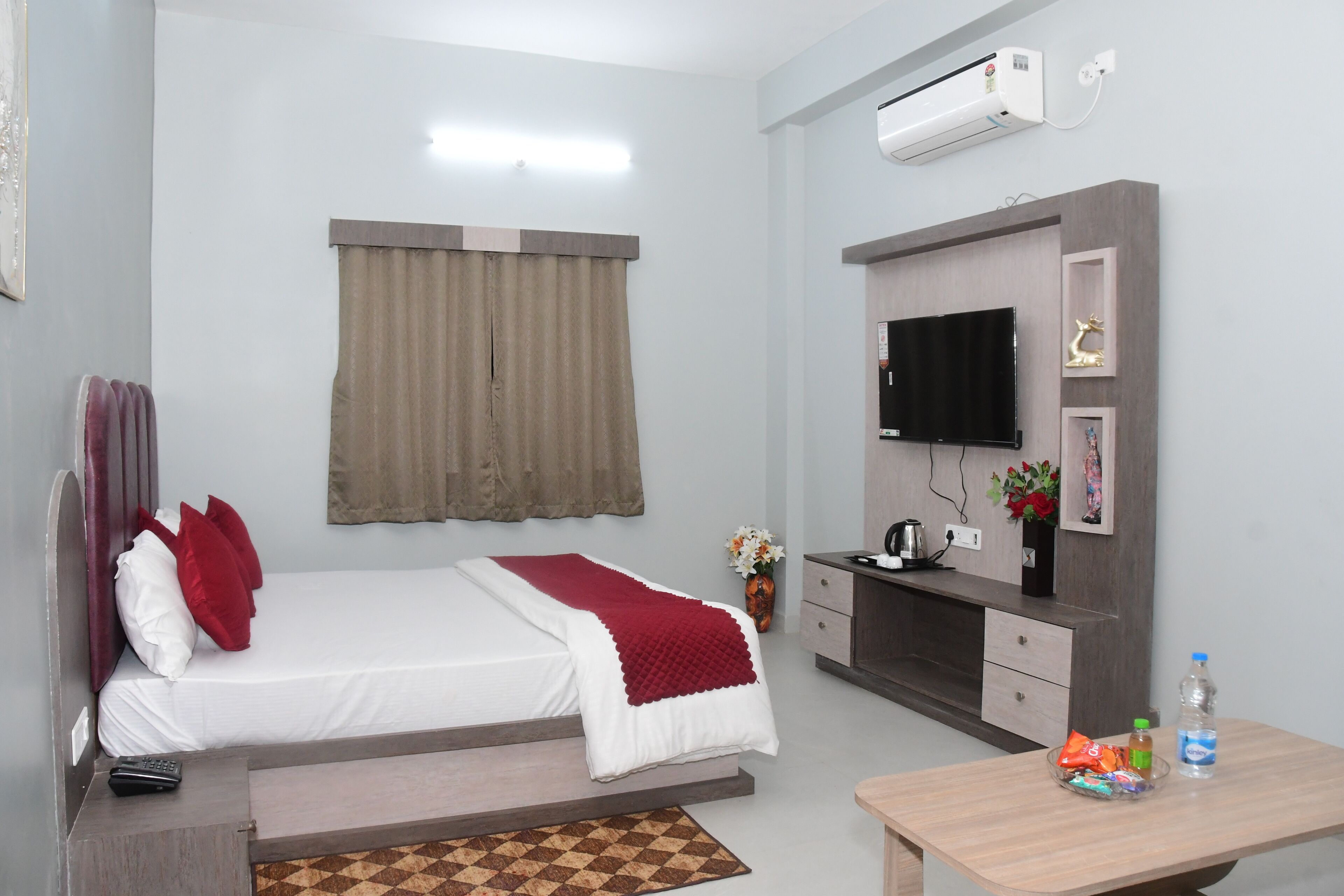 Quarto de hotel com cama, escrivaninha, televisão, janela com cortinas e ar condicionado.