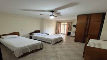 Quarto de hotel com duas camas de solteiro, ventilador de teto, guarda-roupa e uma pequena mesa.