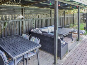 Pátio externo com móveis de vime e uma mesa, sob uma pérgola de madeira com luzes de cordão.