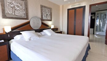 Quarto de hotel com uma cama grande, duas mesinhas de cabeceira, uma cabeceira de madeira e obras de arte nas paredes.