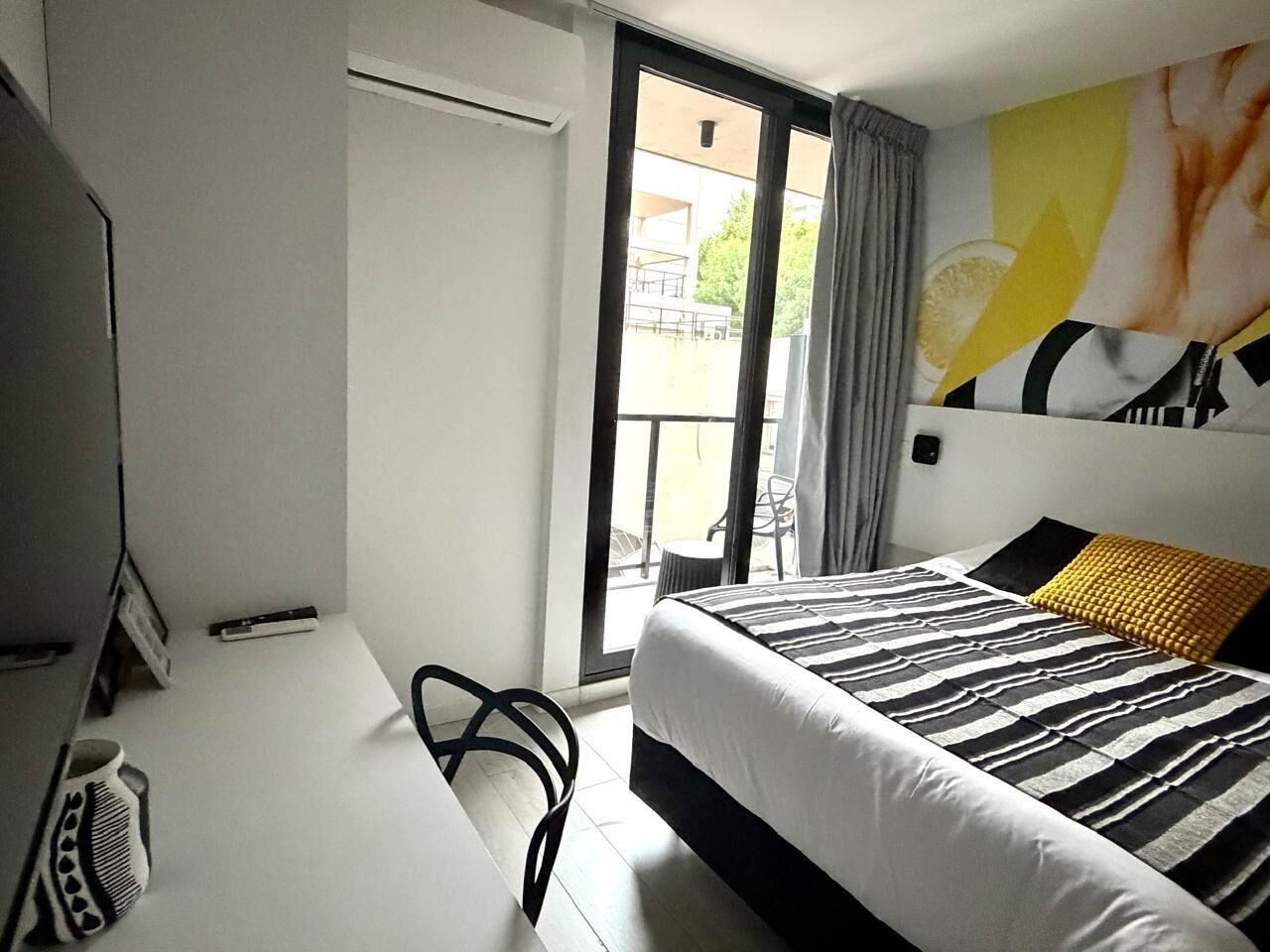 Quarto de hotel com cama, escrivaninha e cadeira. Ampla janela com vista para o exterior.