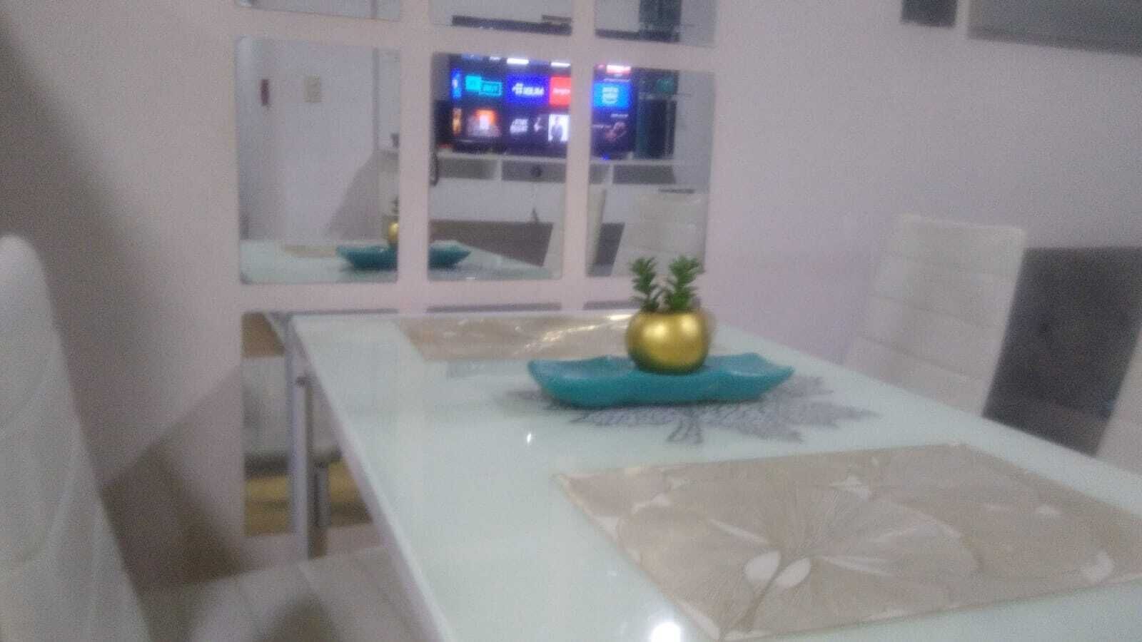 Uma sala de jantar com uma mesa branca, um objeto decorativo dourado e um almofada azul.