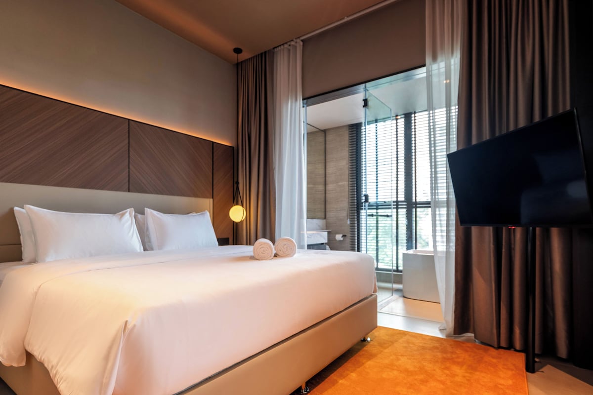 Quarto de hotel moderno com uma cama grande, TV de tela plana e vista para o exterior pela janela.