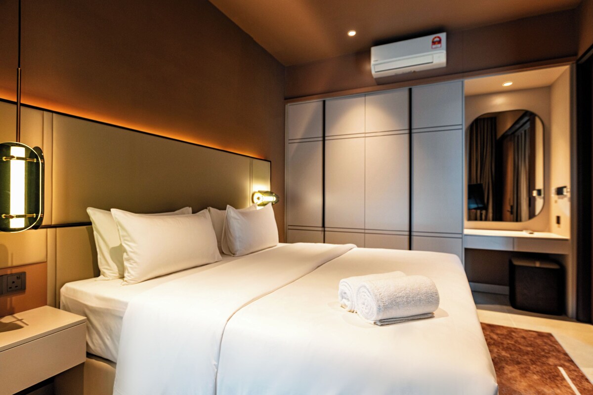 Quarto de hotel com cama bem arrumada, mesa de cabeceira, espelho grande e guarda-roupa.
