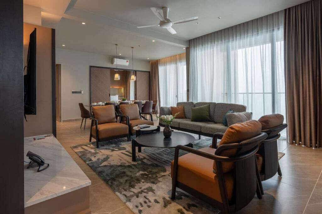 Uma sala de estar moderna com um sofá, poltronas, uma mesa de centro e uma área de jantar ao fundo.