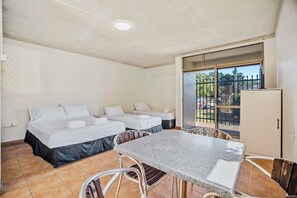 Quarto com duas camas, uma mesa de jantar, cadeiras, um refrigerador e uma porta de vidro corrediça para área externa.