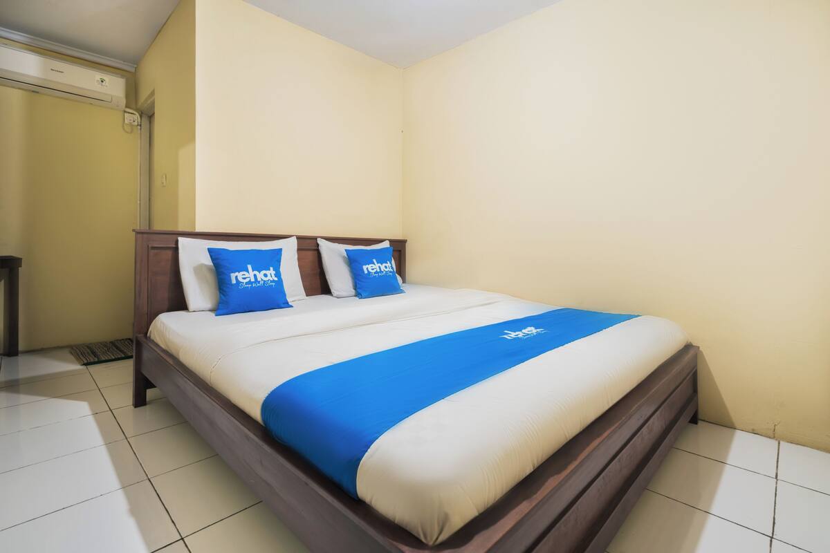 Quarto de hotel com cama, duas almofadas com a marca 'rebot' e um edredom azul, além de cabeceira de madeira.