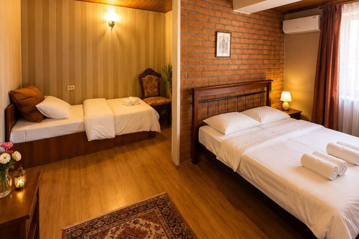 Quarto com duas camas de solteiro, uma cama de casal, piso de madeira, parede decorada com tijolos, teto com iluminação embutida e tapete estampado.