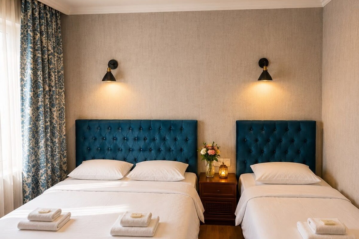 Quarto de hotel com duas camas, cada uma com cabeceira estofada, roupa de cama branca e toalhas dobradas com cuidado.